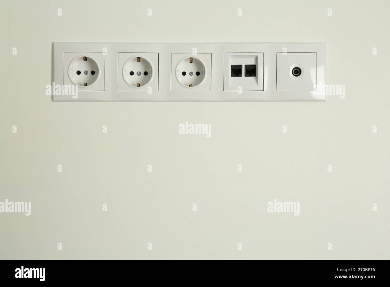 Many power sockets with ethernet and TV coax plates on white wall ...