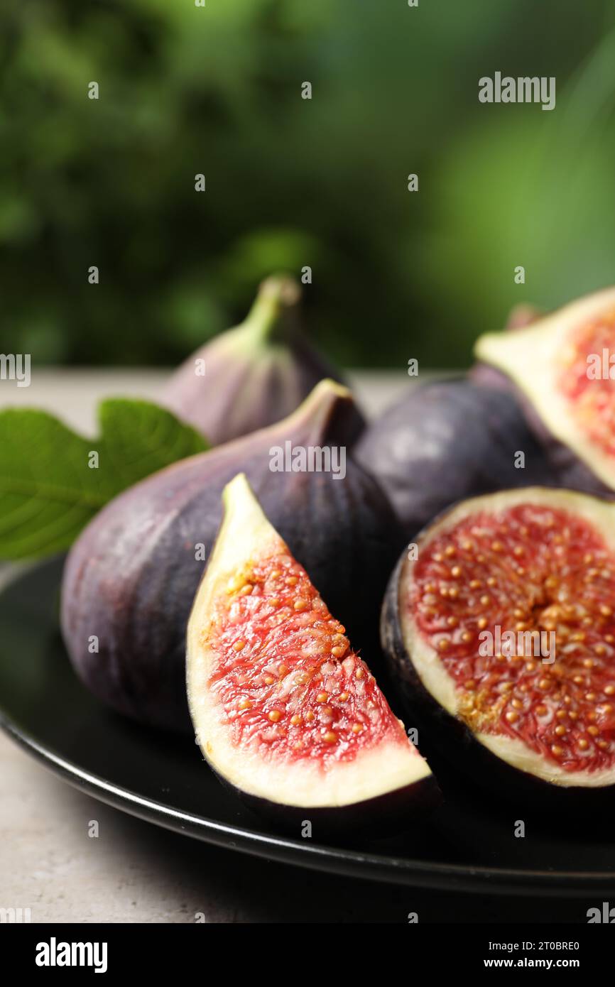 Whole and cut ripe figs on light grey table against blurred green ...