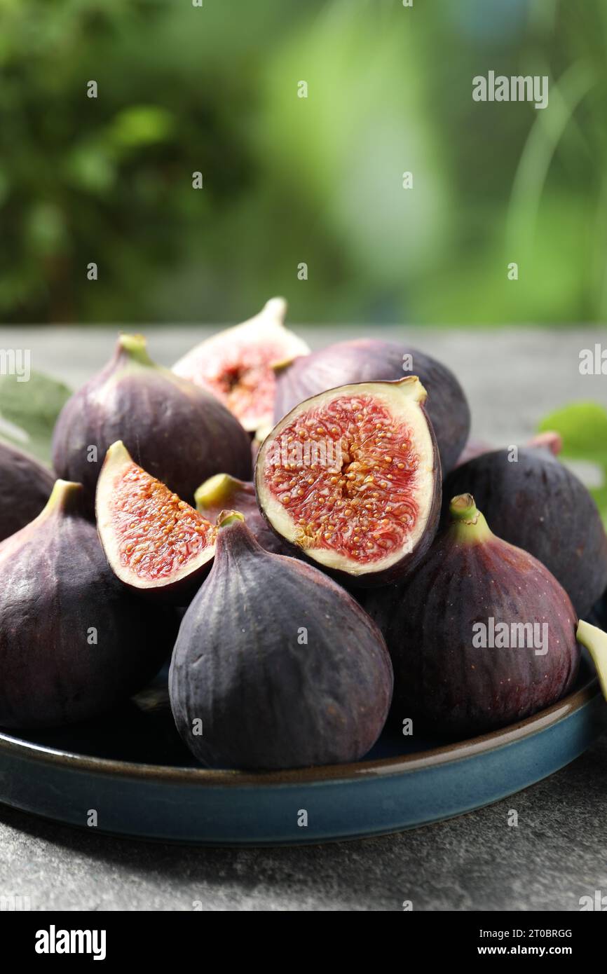 Whole and cut ripe figs on light grey textured table against blurred ...