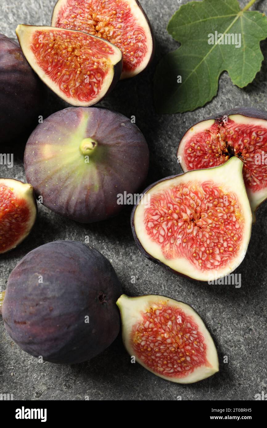 Whole and cut ripe figs with leaf on grey textured table, flat lay ...