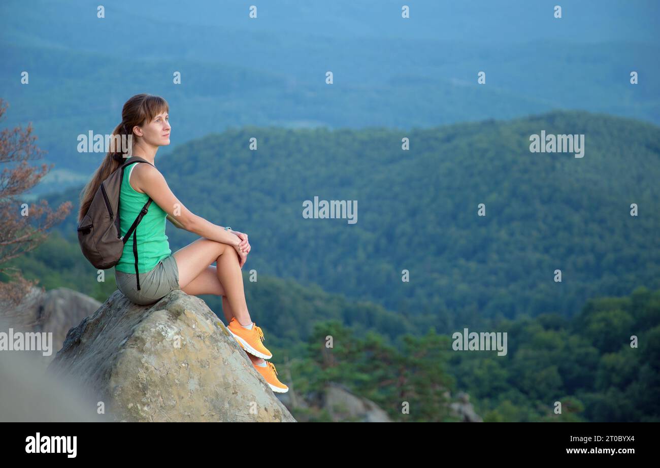 Hiker woman resting on rocky mountain top enjoying summer nature during ...