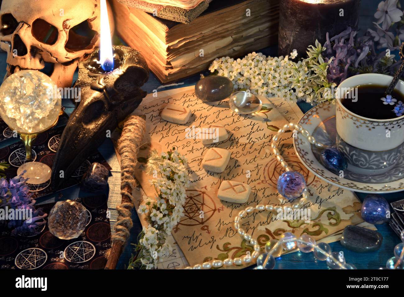 Burning black candle, skull, runes and crystals on witch altar table ...