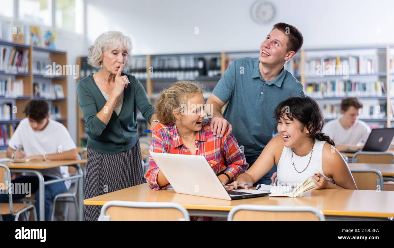Mature teacher urges noisy teenagers to be quiet in school library ...