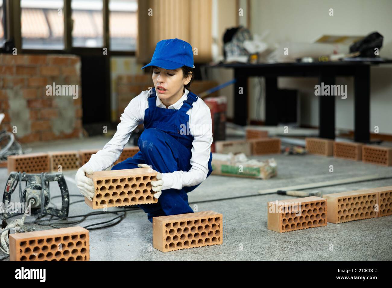 Female builder arranging bricks inside building under construction ...