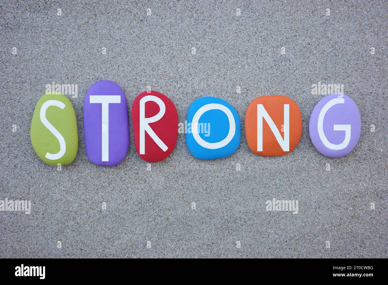 Strong word composed with multi colored stone letters over beach sand ...