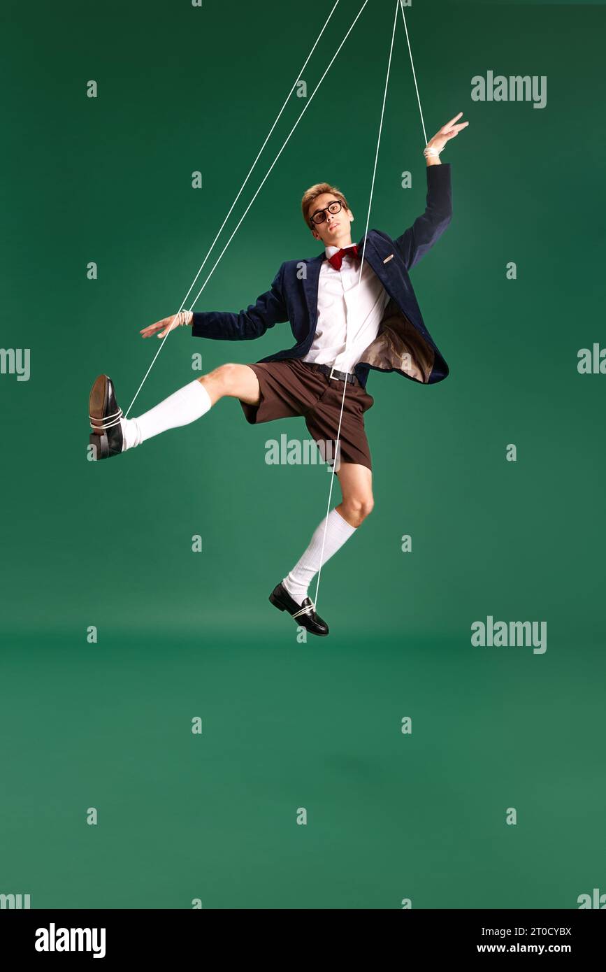 Young guy, marionette on string in motion against green studio ...