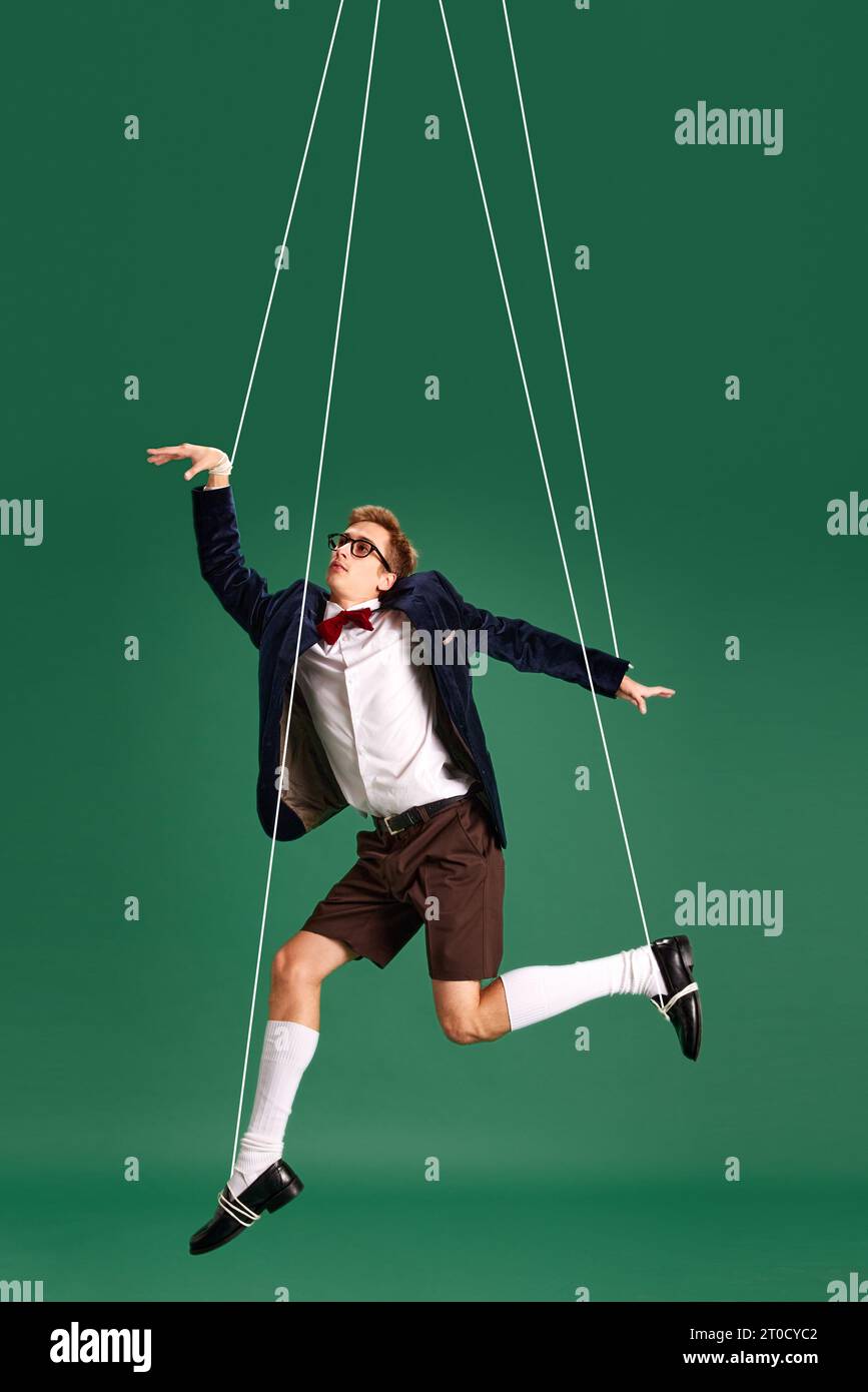 Young guy, marionette on string in motion against green studio ...