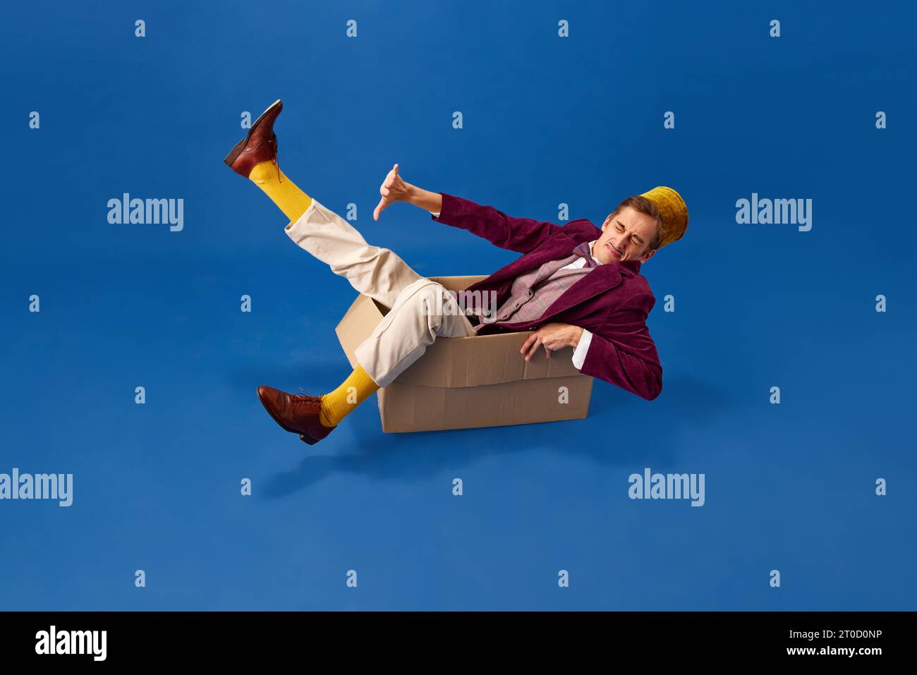 Young guy, porter sitting in box with eyes closed against blue studio ...