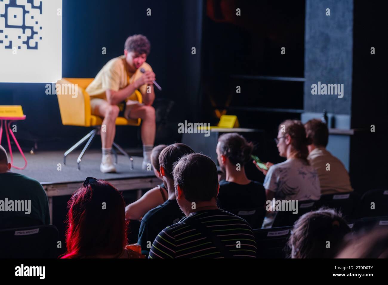 Blurred male coach sitting on chair on stage, near screen and answering ...