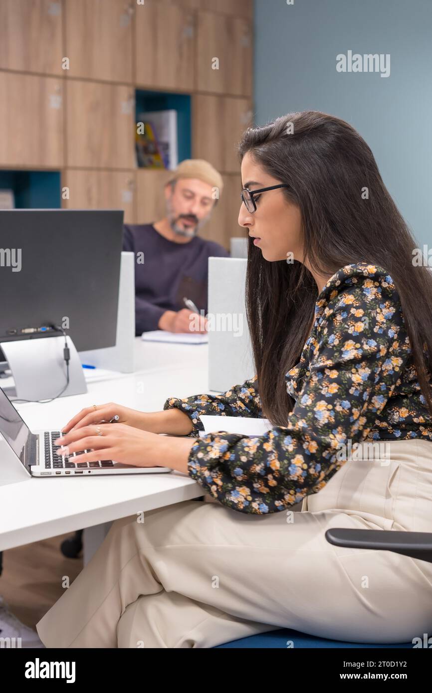 Vertical photo of a woman using laptop while working next to colleagues ...