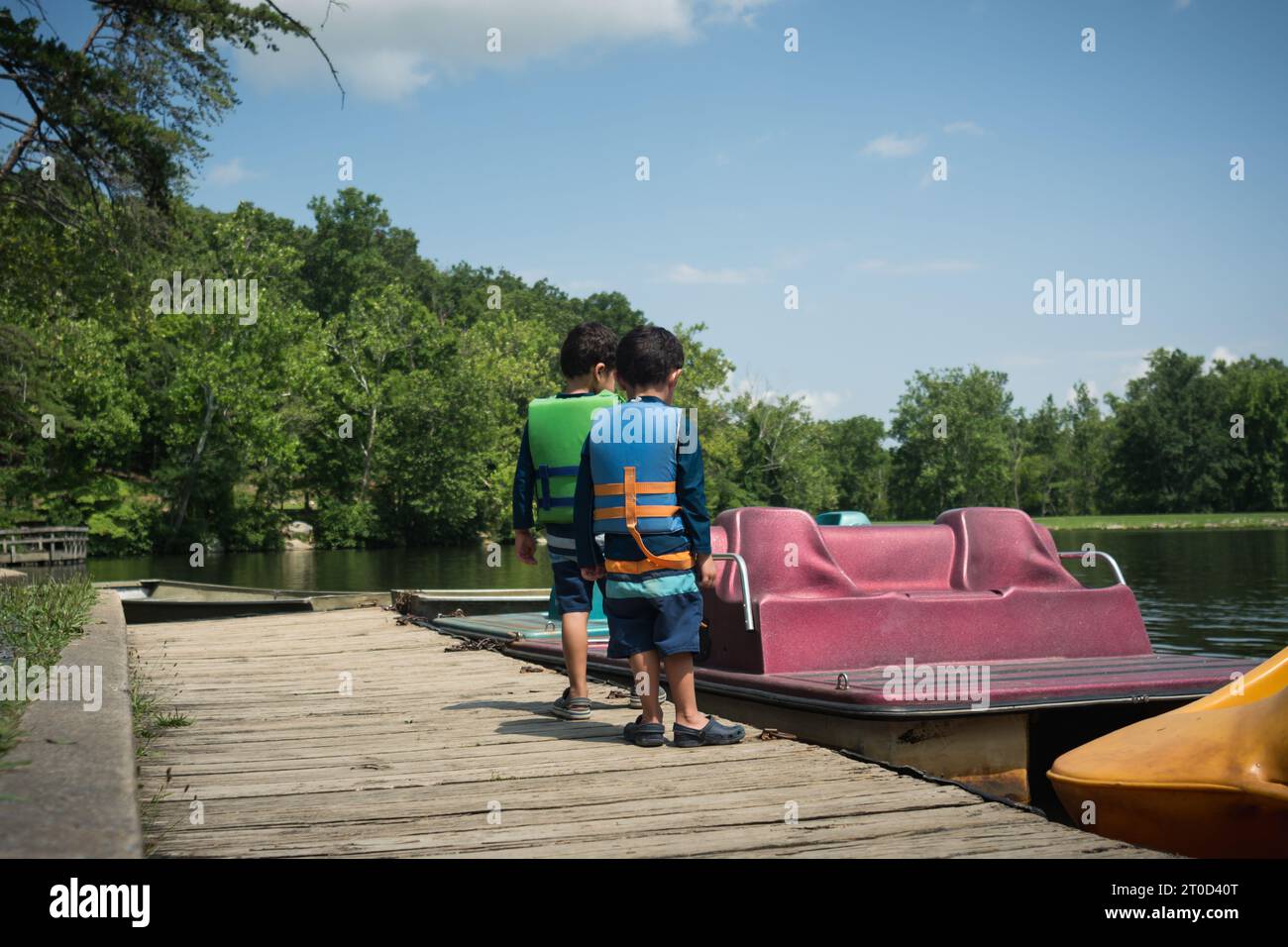 Two young boys standing on wooden dock by paddleboat in lake Stock ...
