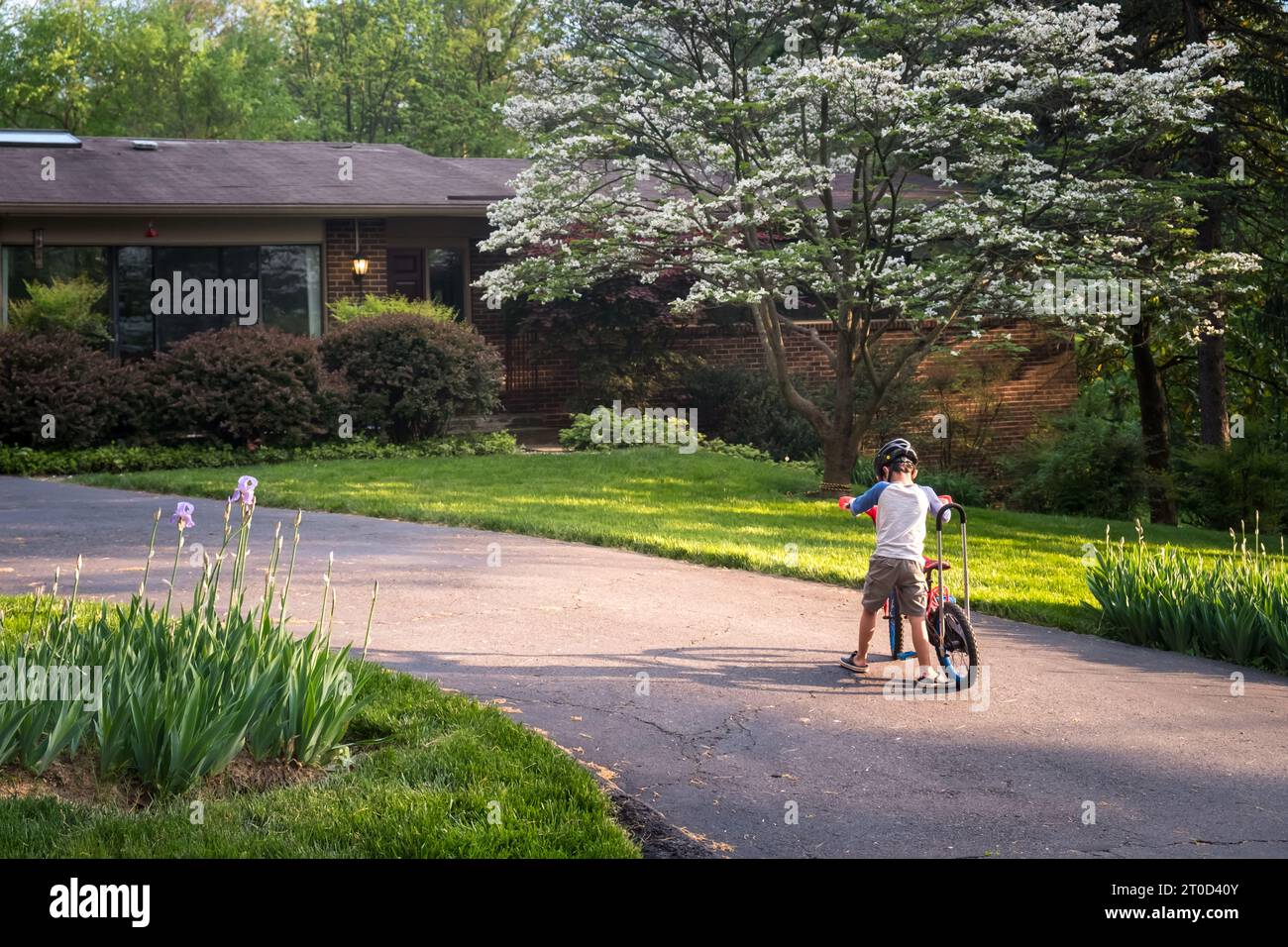 Boy pushing bicycle up driveway in suburban neighborhood Stock Photo ...