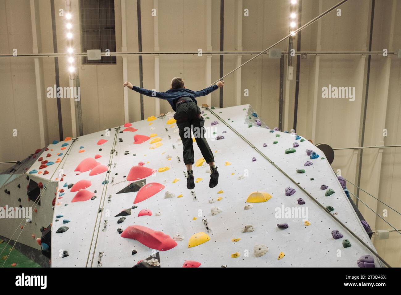 boy lying back off a climbing wall whilst climbing at an indoor gym ...