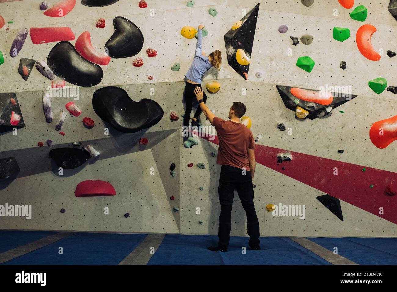 dad helping his daughter climb a bouldering wall at a climbing centre ...