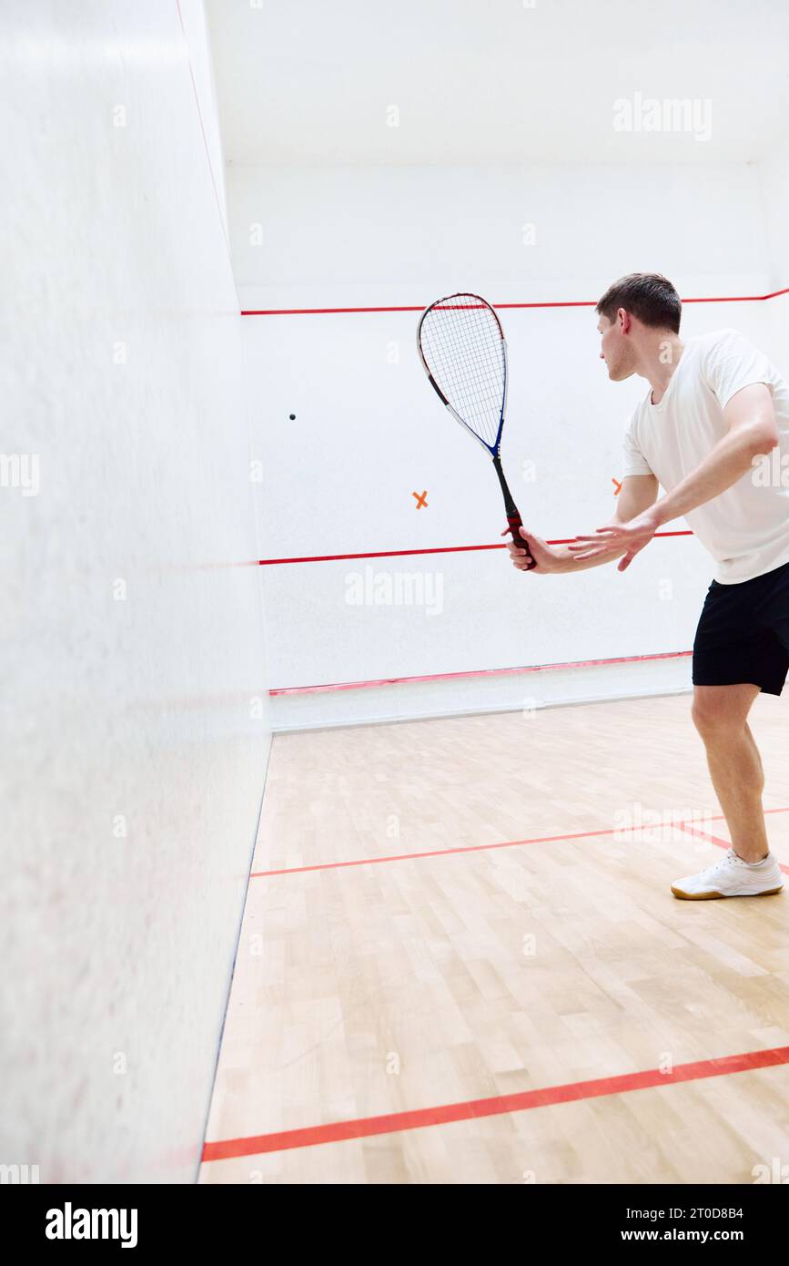 Young sportive man playing, training squash on squash court. Hitting ...