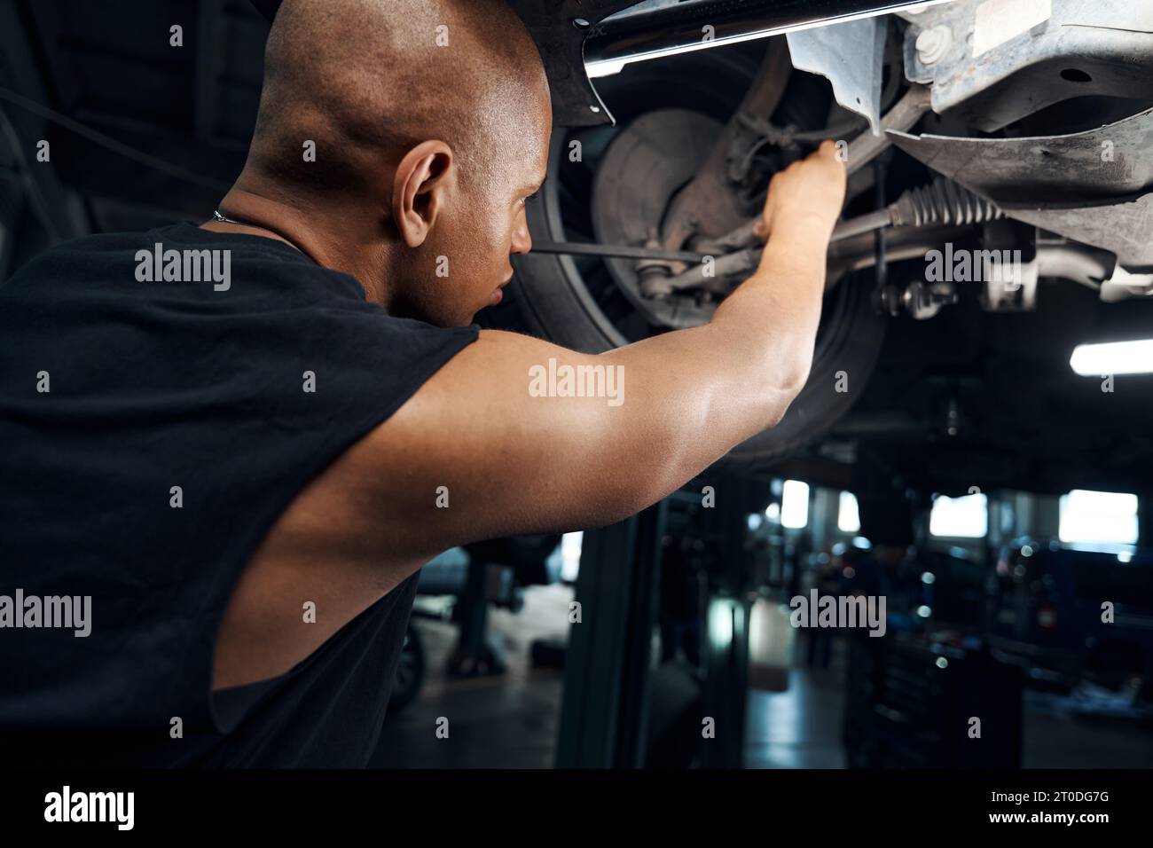 African American mechanic working under the car using long screwdriver ...