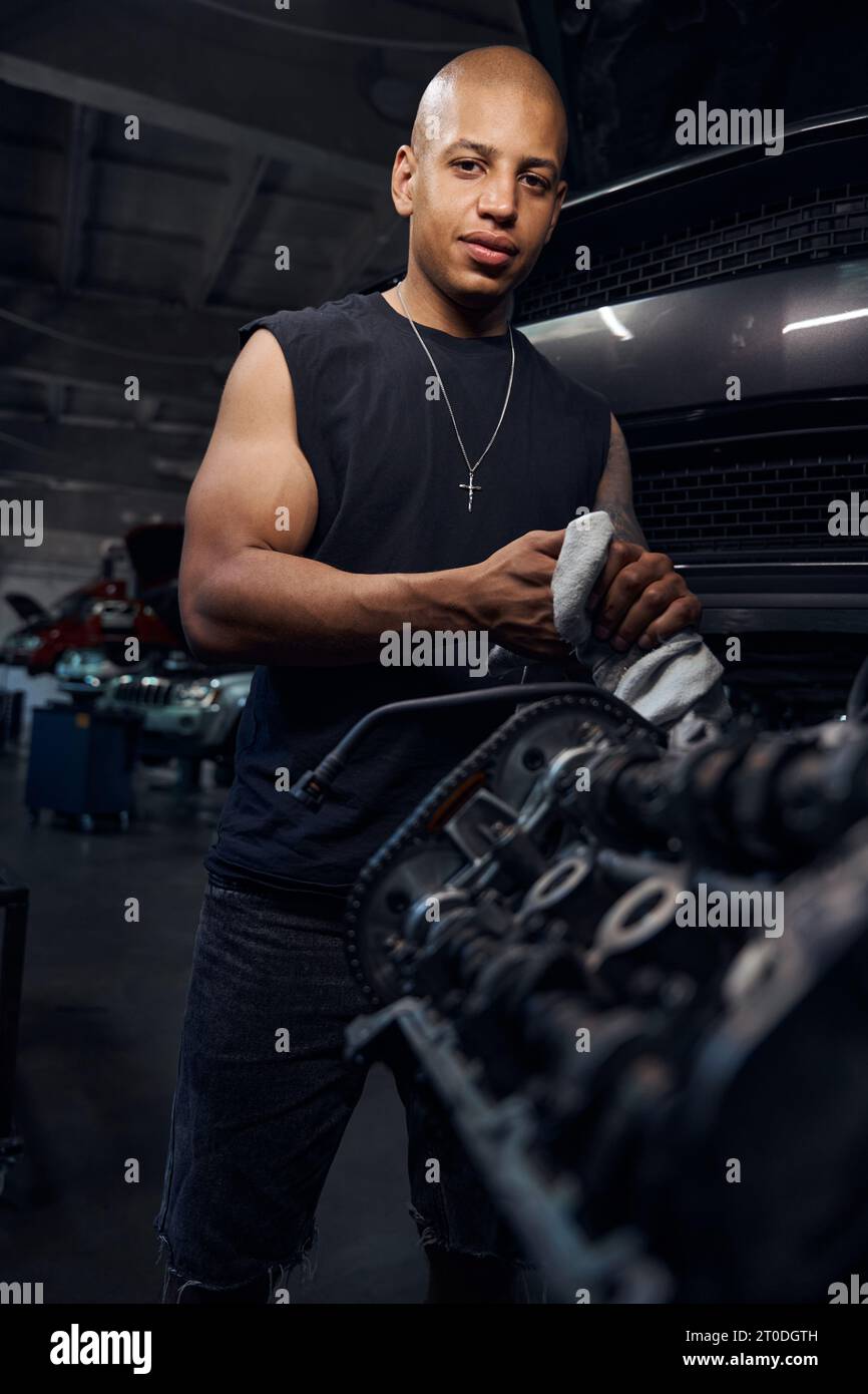 Smiling auto-mechanic cleaning hands after successful engine repairing ...