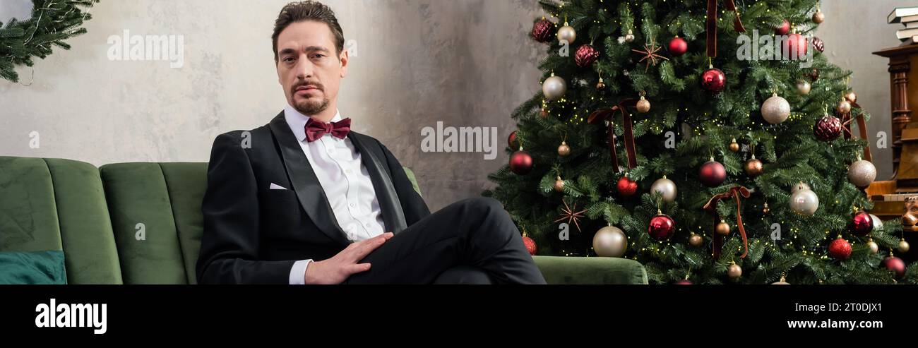 well-dressed man with beard wearing tuxedo with bow tie sitting on sofa ...