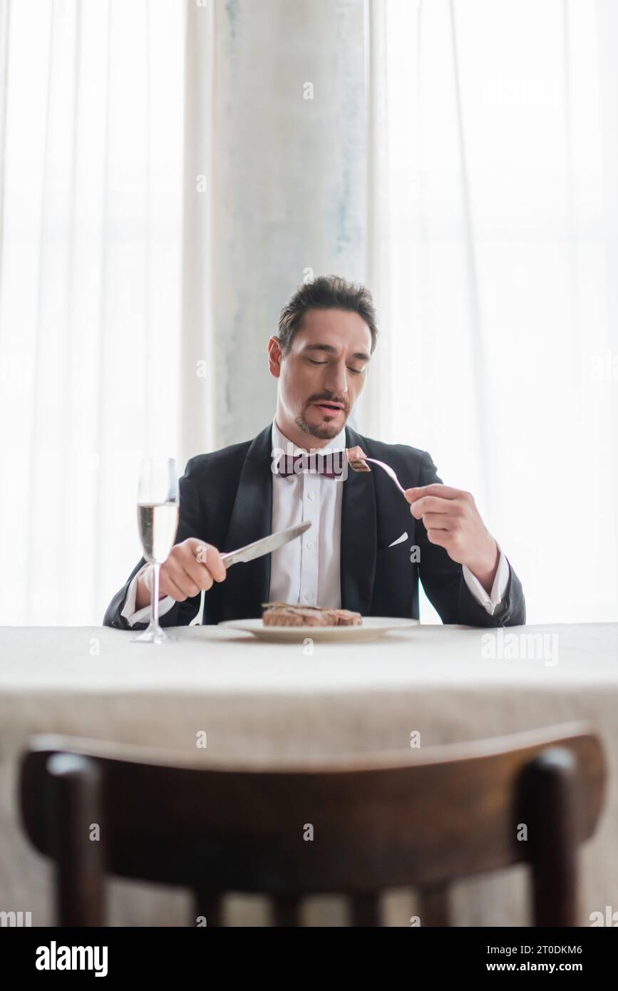 well-dressed gentleman in tuxedo eating delicious beef steak near glass ...