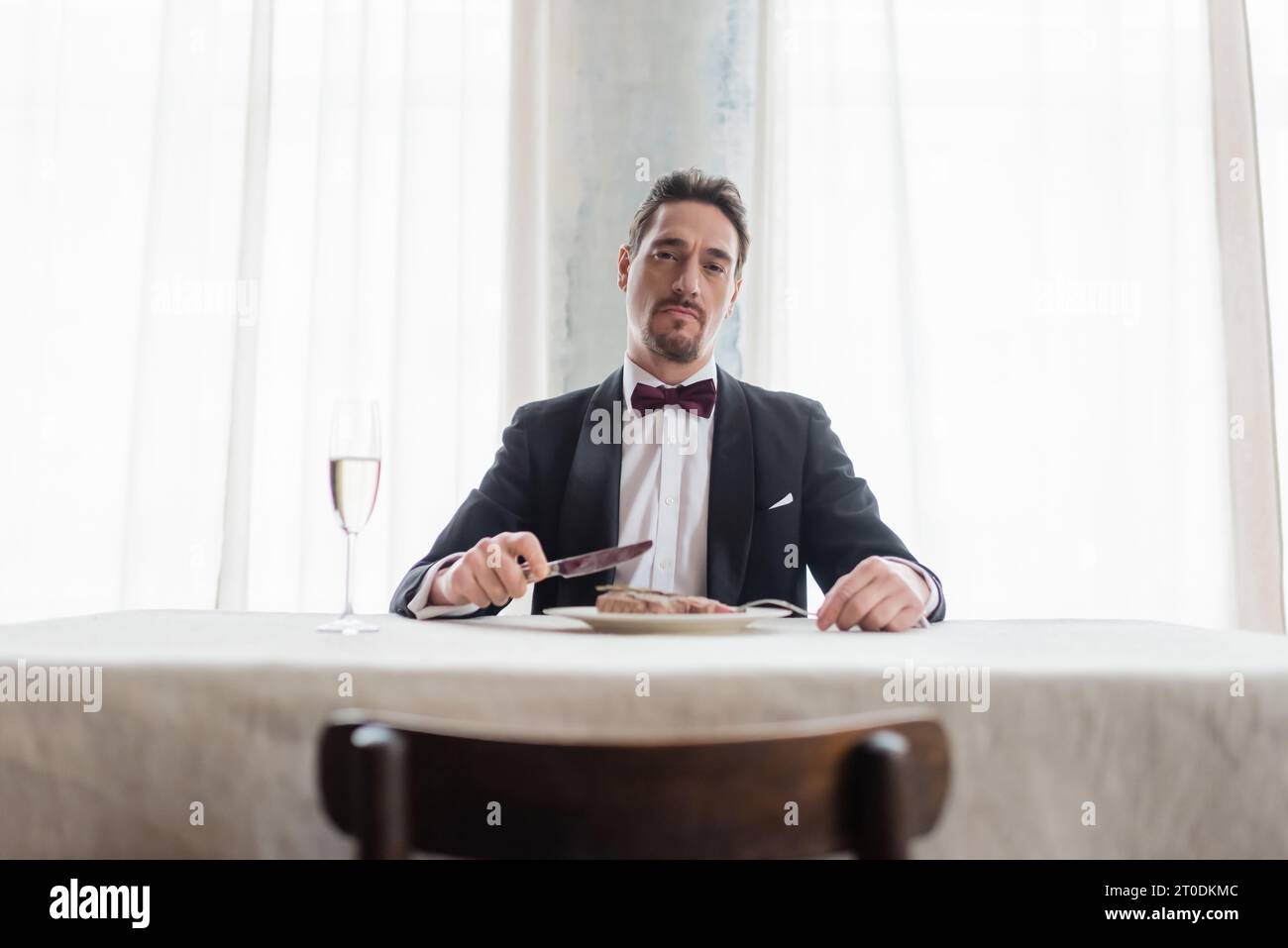 wealthy gentleman in tuxedo eating delicious beef steak near glass of ...
