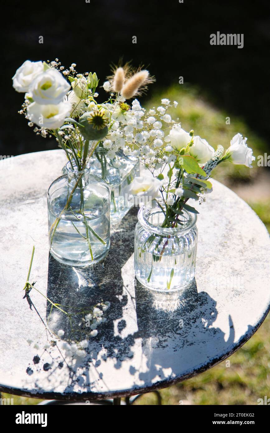 Two summer flower bouquets in small glass vases on round outdoor table ...