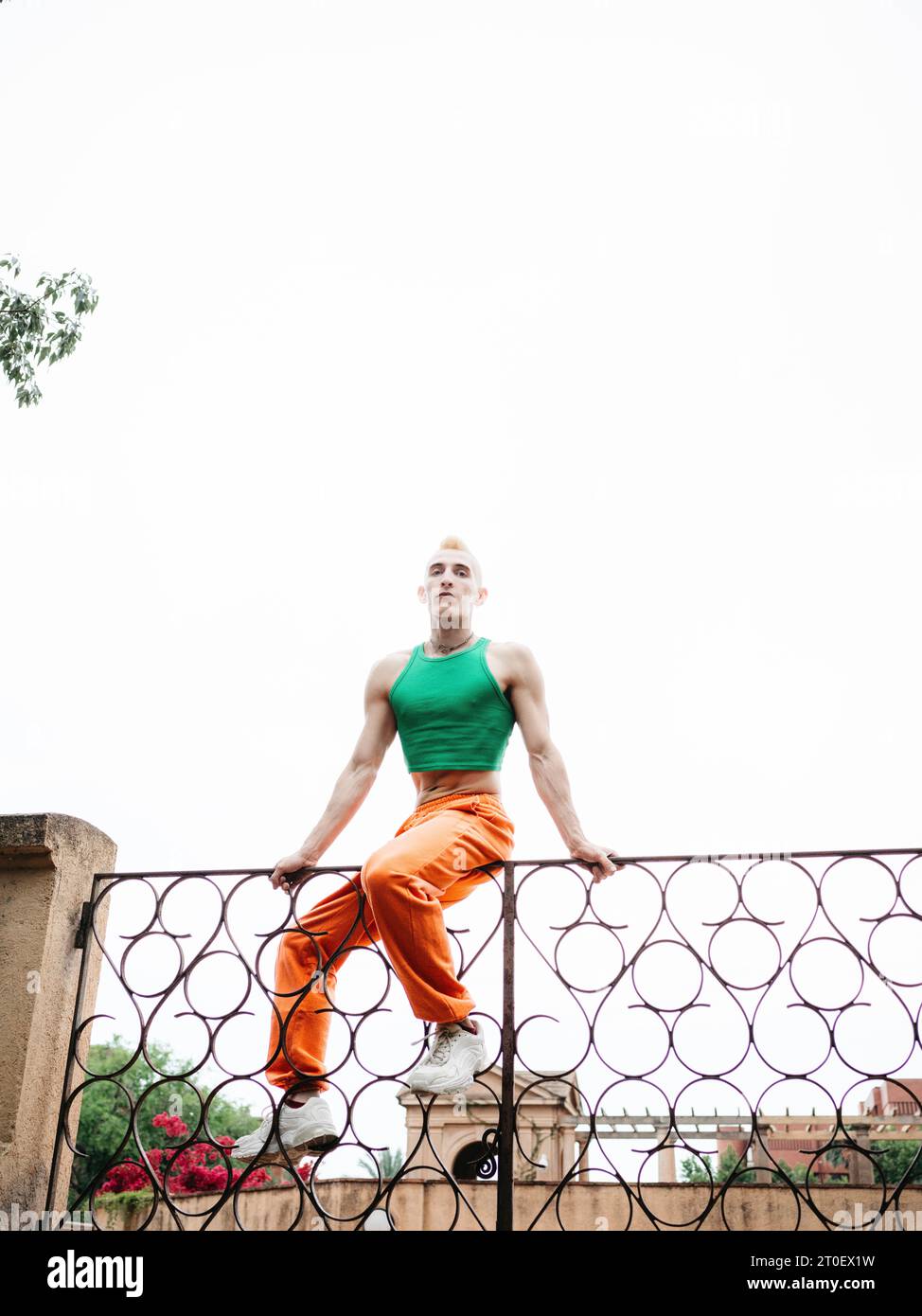 Non-binary human with green top and orange pants climbs a fence Stock ...