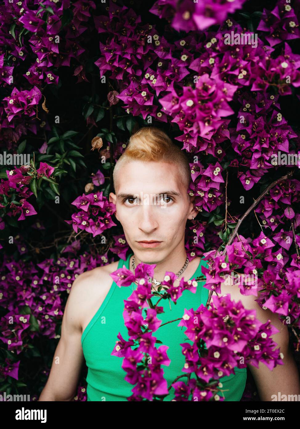 Non-binary person with green top stands in front of shrub with flowers ...