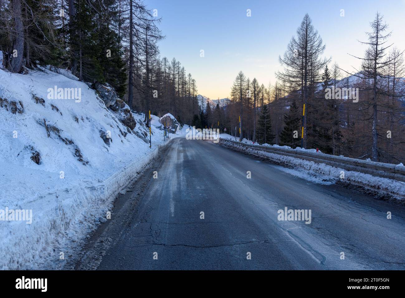 Icy winding alpine road through a snowy forest at dusk in winter Stock ...