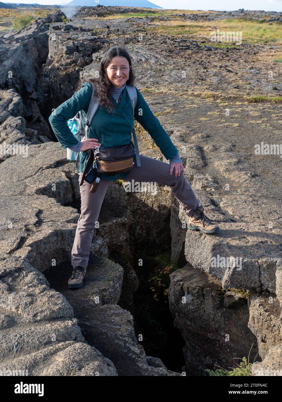 Smiling woman straddling an extension fracture at Grjótagjá between ...