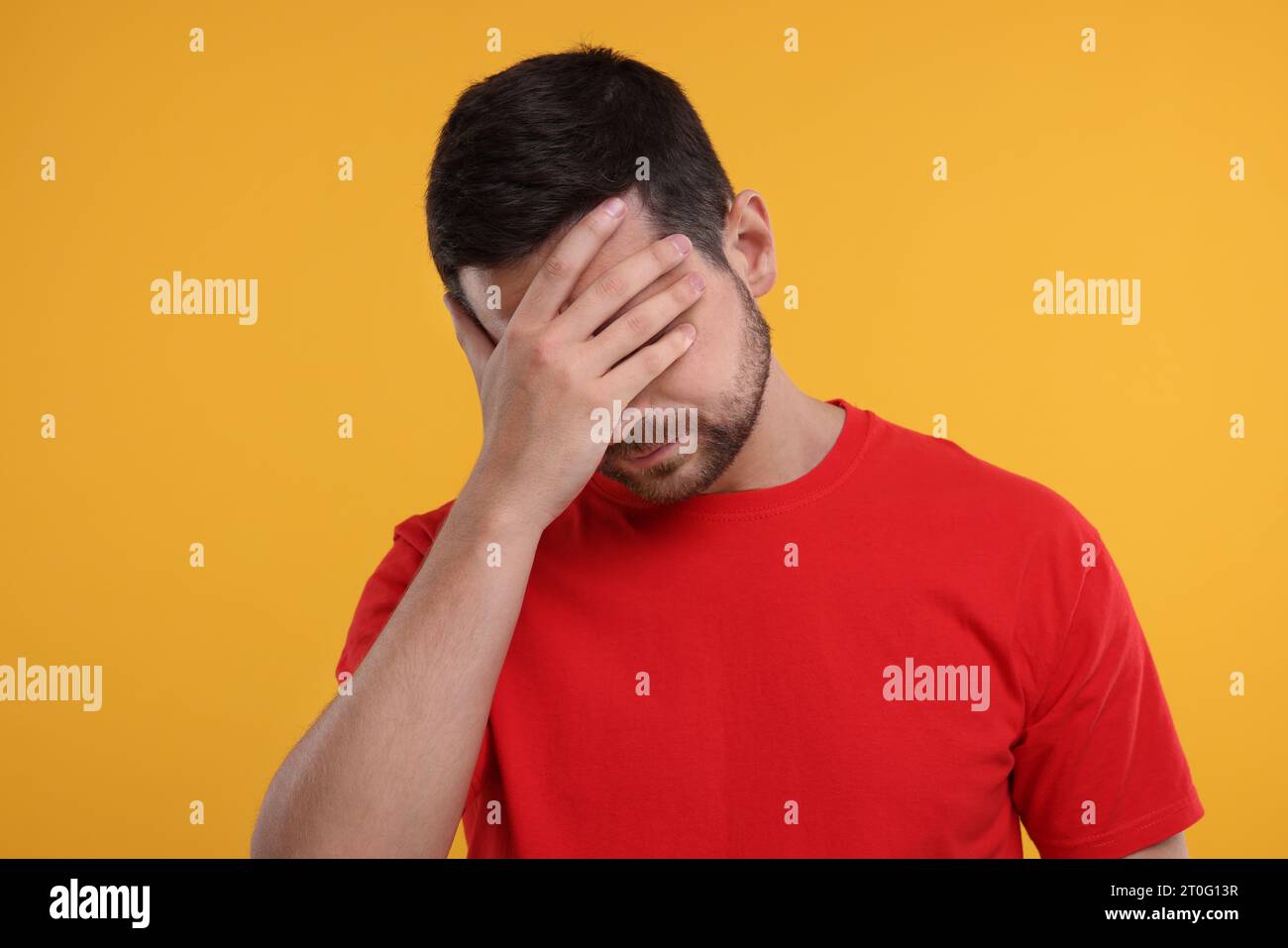 Embarrassed man covering face on orange background Stock Photo - Alamy