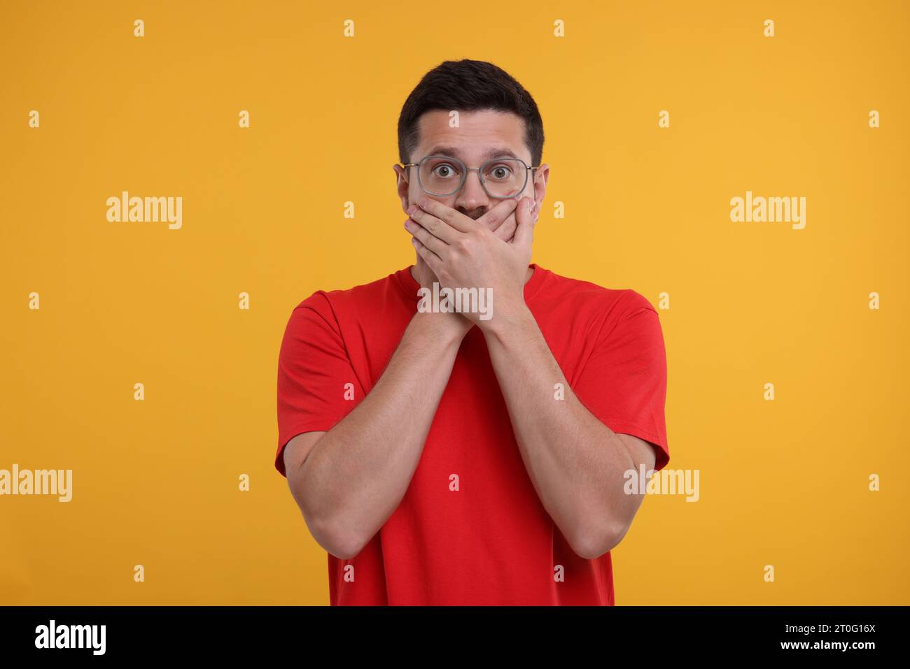 Embarrassed man covering mouth on orange background Stock Photo - Alamy