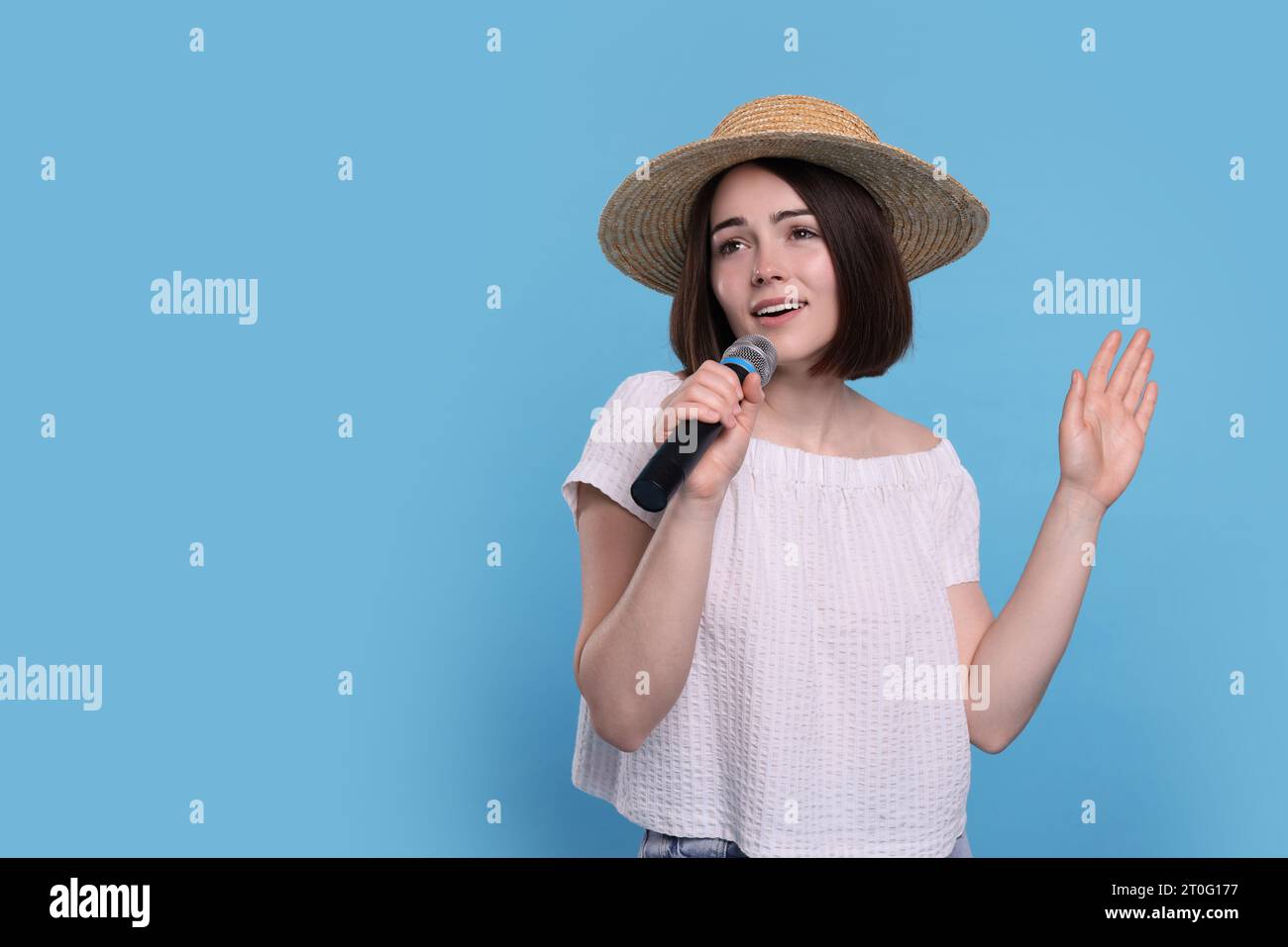 Beautiful woman in hat with microphone singing on light blue background ...