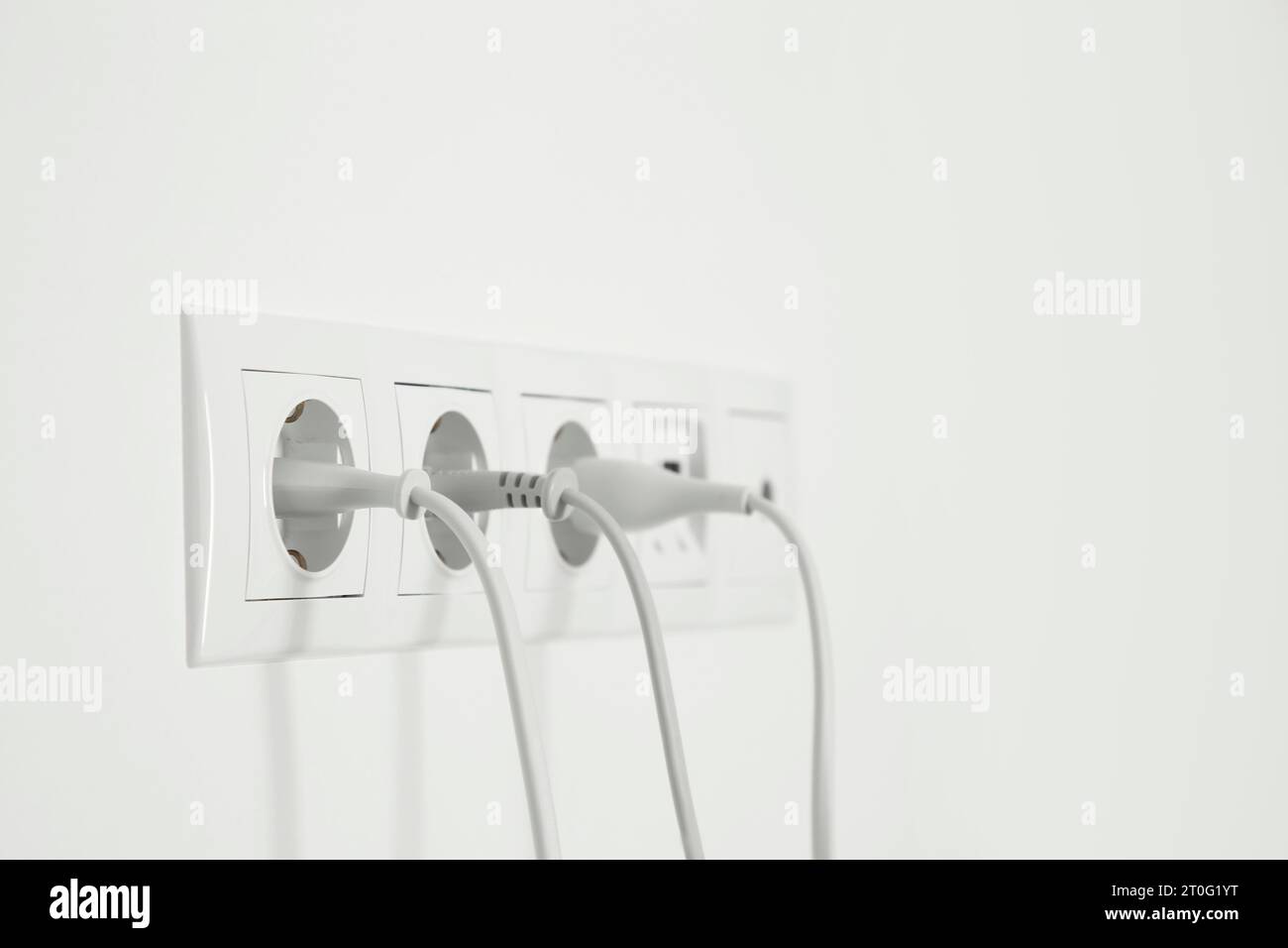 Many power sockets with plugs on white wall indoors. Space for text ...
