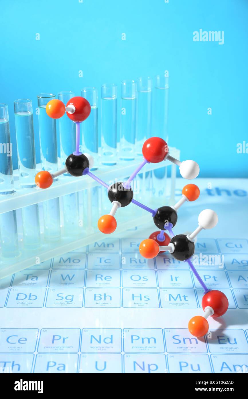 Molecular model and test tubes on periodic table against light blue ...