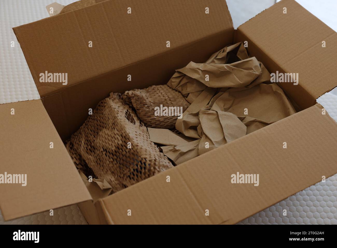 Open cardboard box with crumpled brown paper filler on white mattress ...