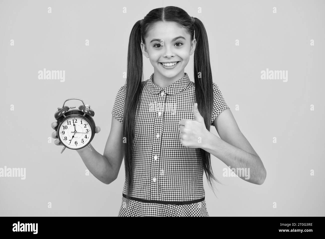 Happy teenager teen girl holding clock over yellow background. Early ...