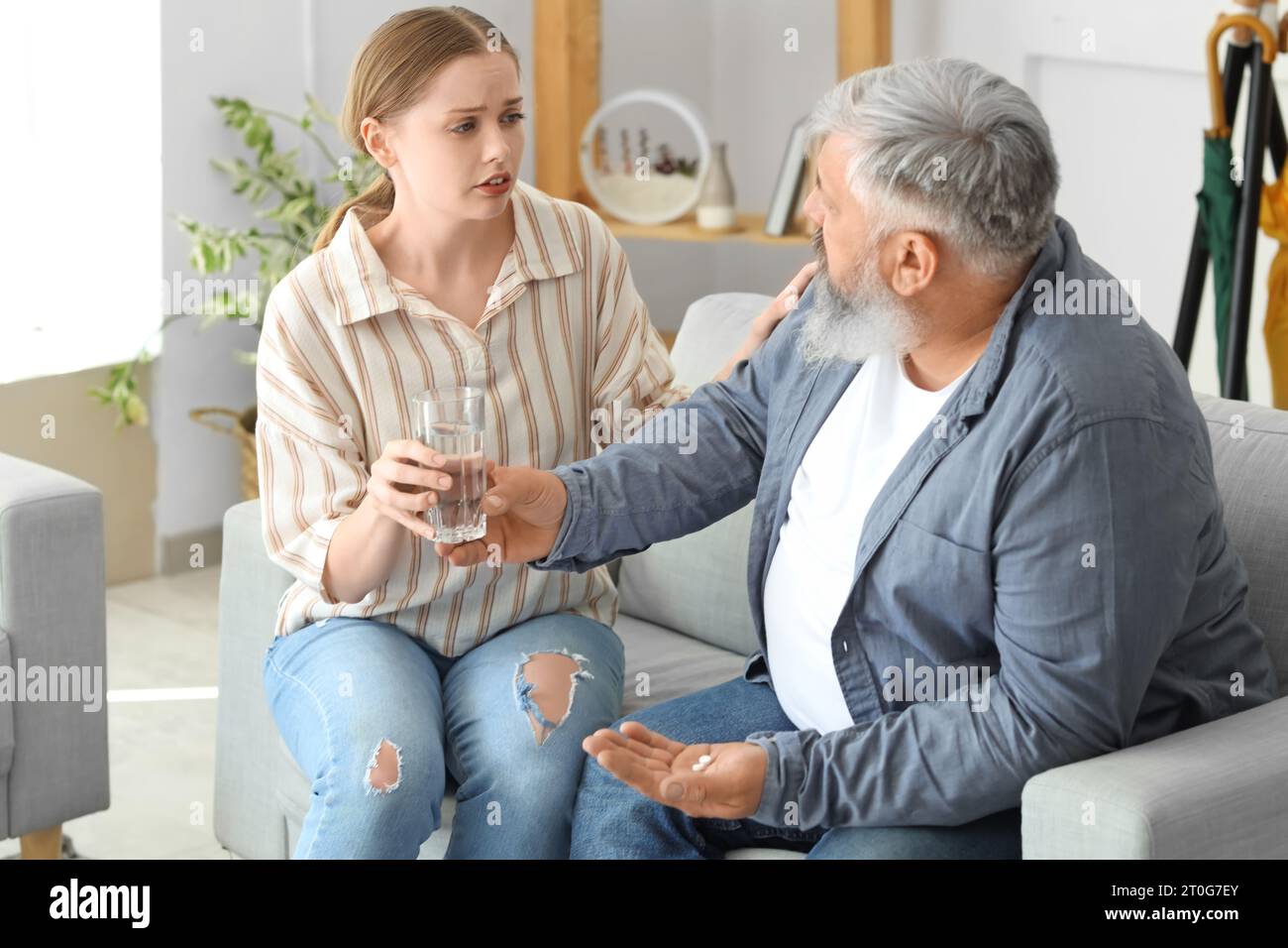 Young woman giving medicine to her father who is having heart attack at ...