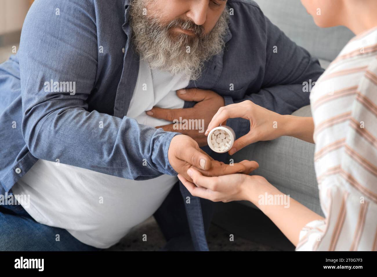 Young woman giving medicine to her father who is having heart attack at ...