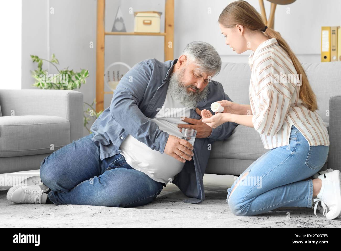Young woman giving medicine to her father who is having heart attack at ...