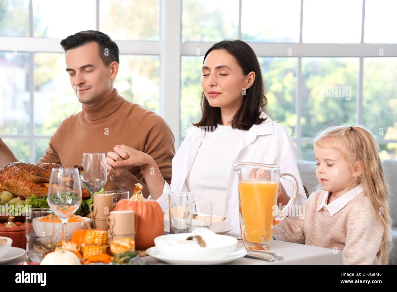 Happy family praying before dinner at festive table on Thanksgiving Day ...