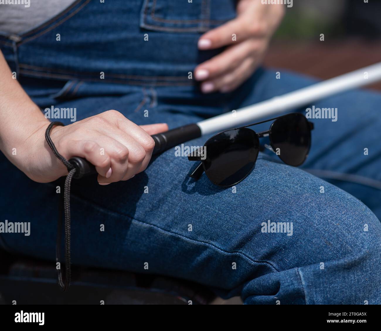 A blind pregnant woman sits on a bench and holds a folding tactile cane ...