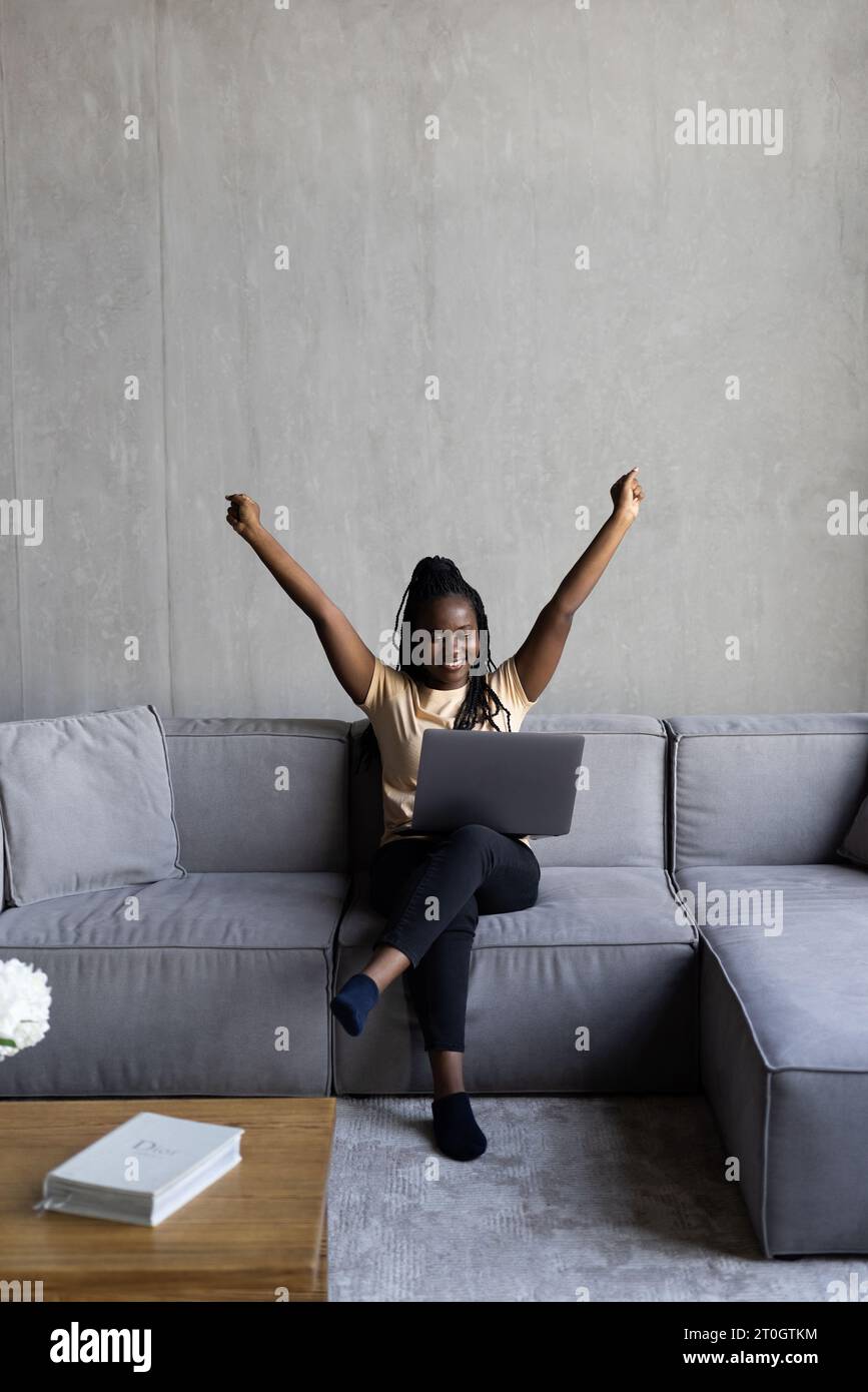 Excited cheerful young Black woman using laptop computer on sofa at ...