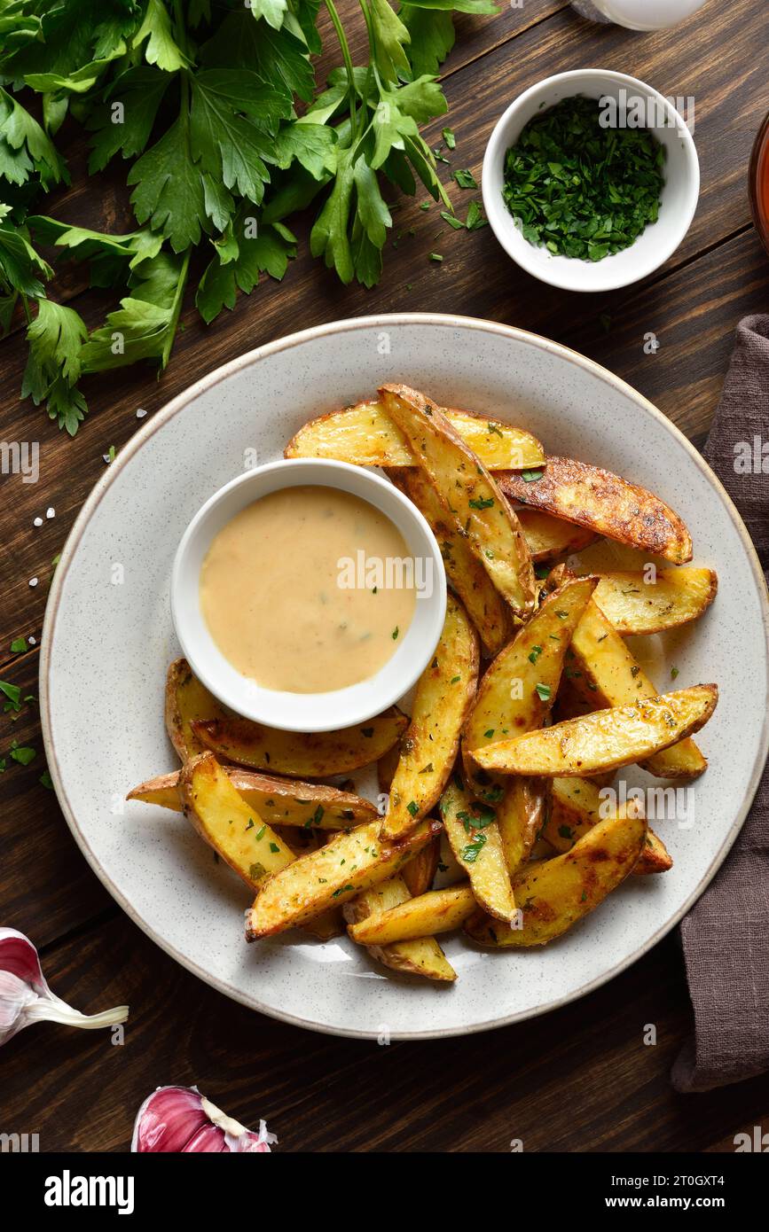 Baked potato wedges with dipping sauce over wooden background. Top view ...