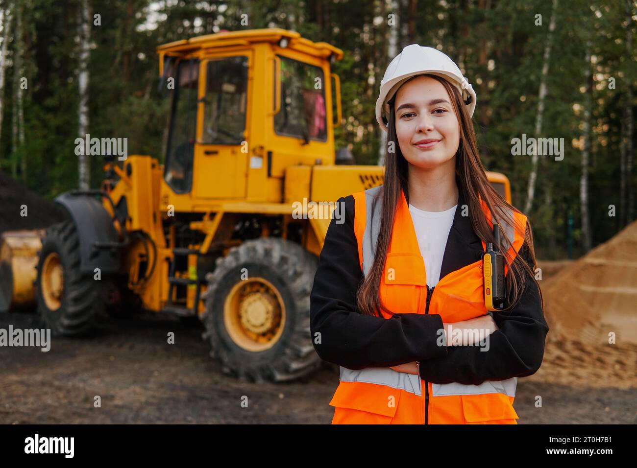 A young woman mine worker is standing in front of a large dump truck or ...