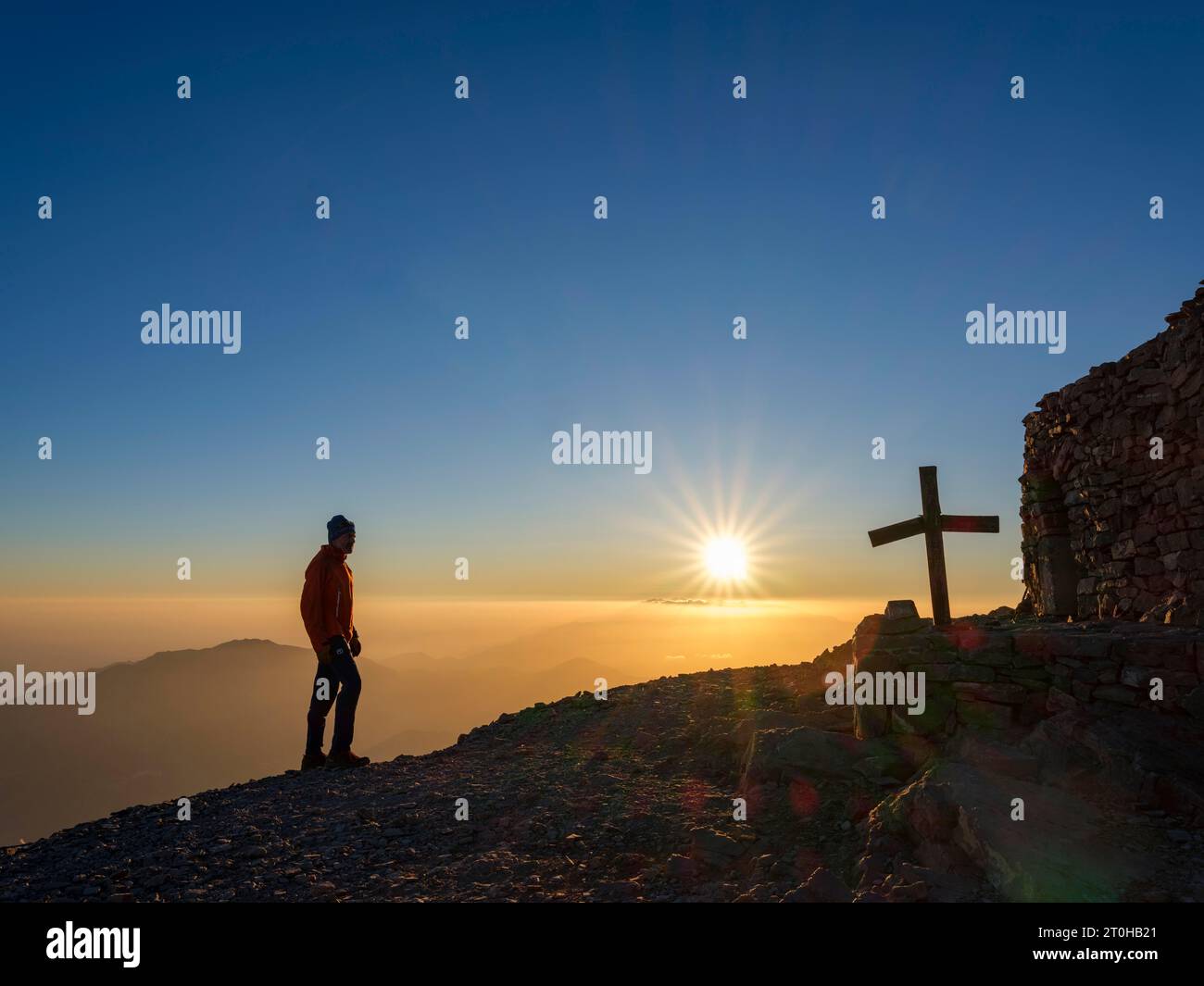 Mountaineer standing at sunset next to summit chapel Timios Stavros and ...