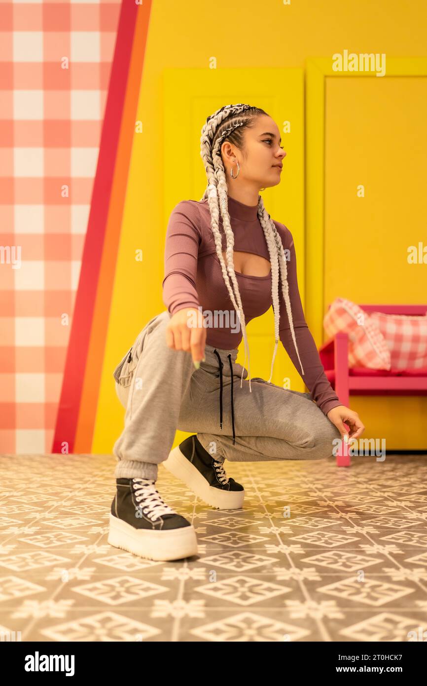 Young girl with white braids on a yellow background, crouching in an ...