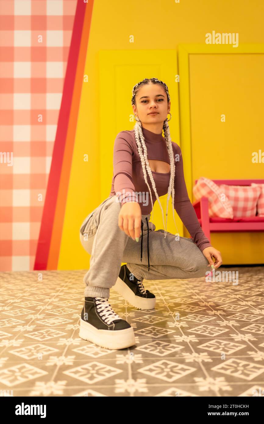 Young girl with white braids on a yellow background, crouching in an ...