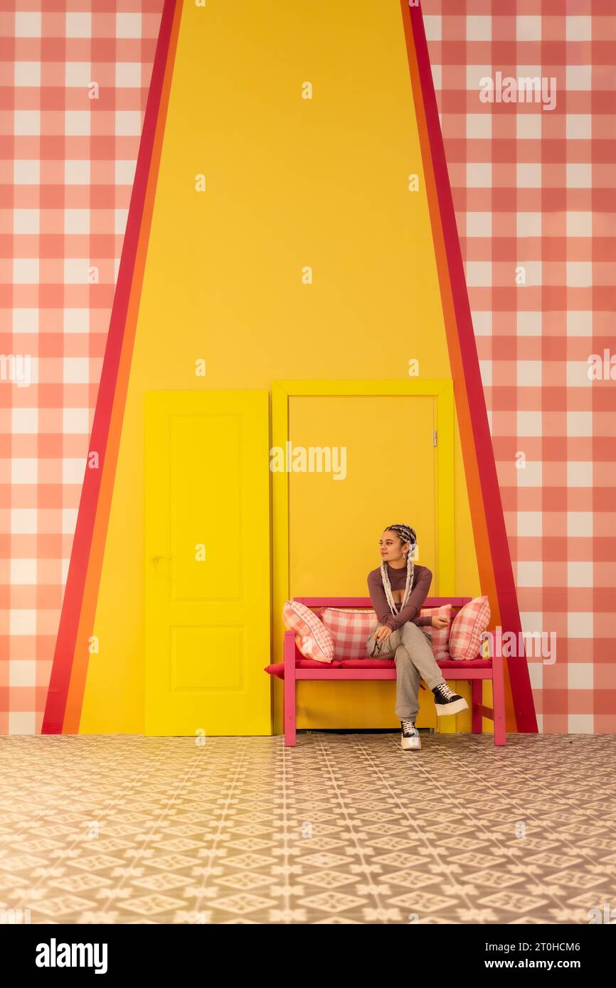 Young girl with white braids on a yellow background, sitting on a pink ...