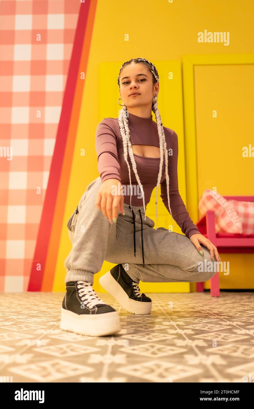 Young girl with white braids on a yellow background, crouching in an ...