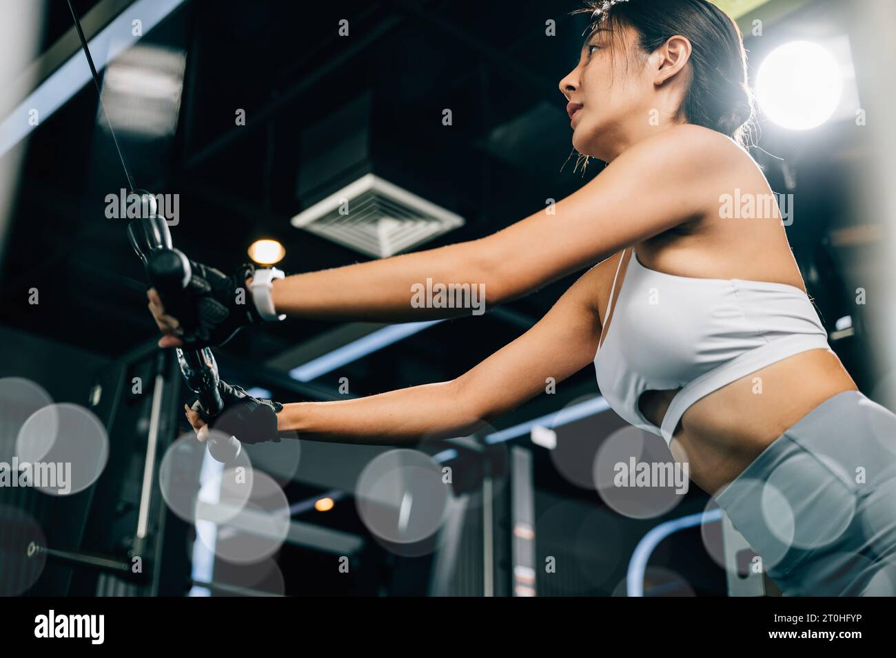 Slim and strong young woman working out on a pull-down weight machine ...